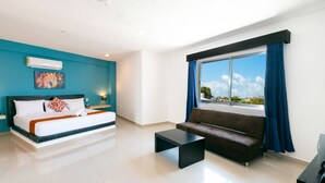 Quarto de hotel moderno com uma cama grande, um sofá, uma mesa de centro e vista para o exterior através de uma janela ampla.