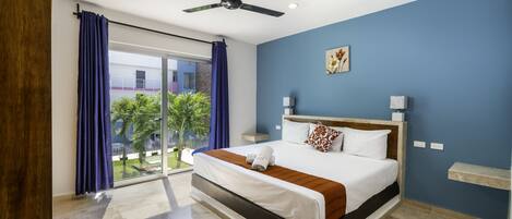 Quarto de hotel moderno com uma cama grande, ventoinha no teto, vista para o exterior e parede azul como detalhe.