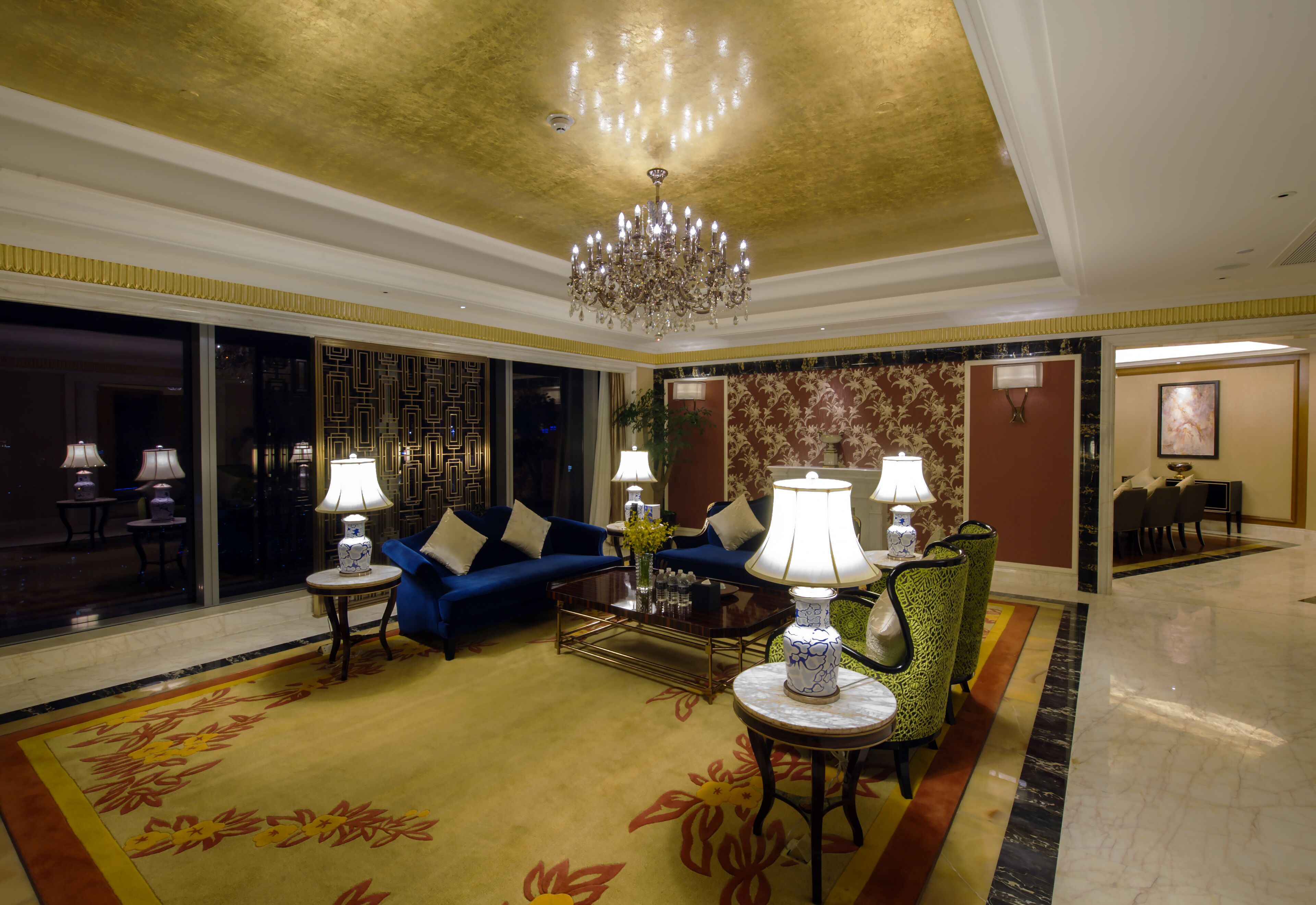 Um hall amplo com um sofá azul, duas luminárias, um candelabro e um tapete estampado.