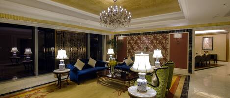 Um hall amplo com um sofá azul, duas luminárias, um candelabro e um tapete estampado.