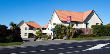 Um motel de dois andares com telhado de telhas vermelhas, uma placa e um gramado bem cuidado.