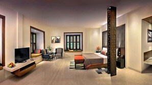 Quarto de hotel moderno com cama, área de estar, televisão e janelas amplas.