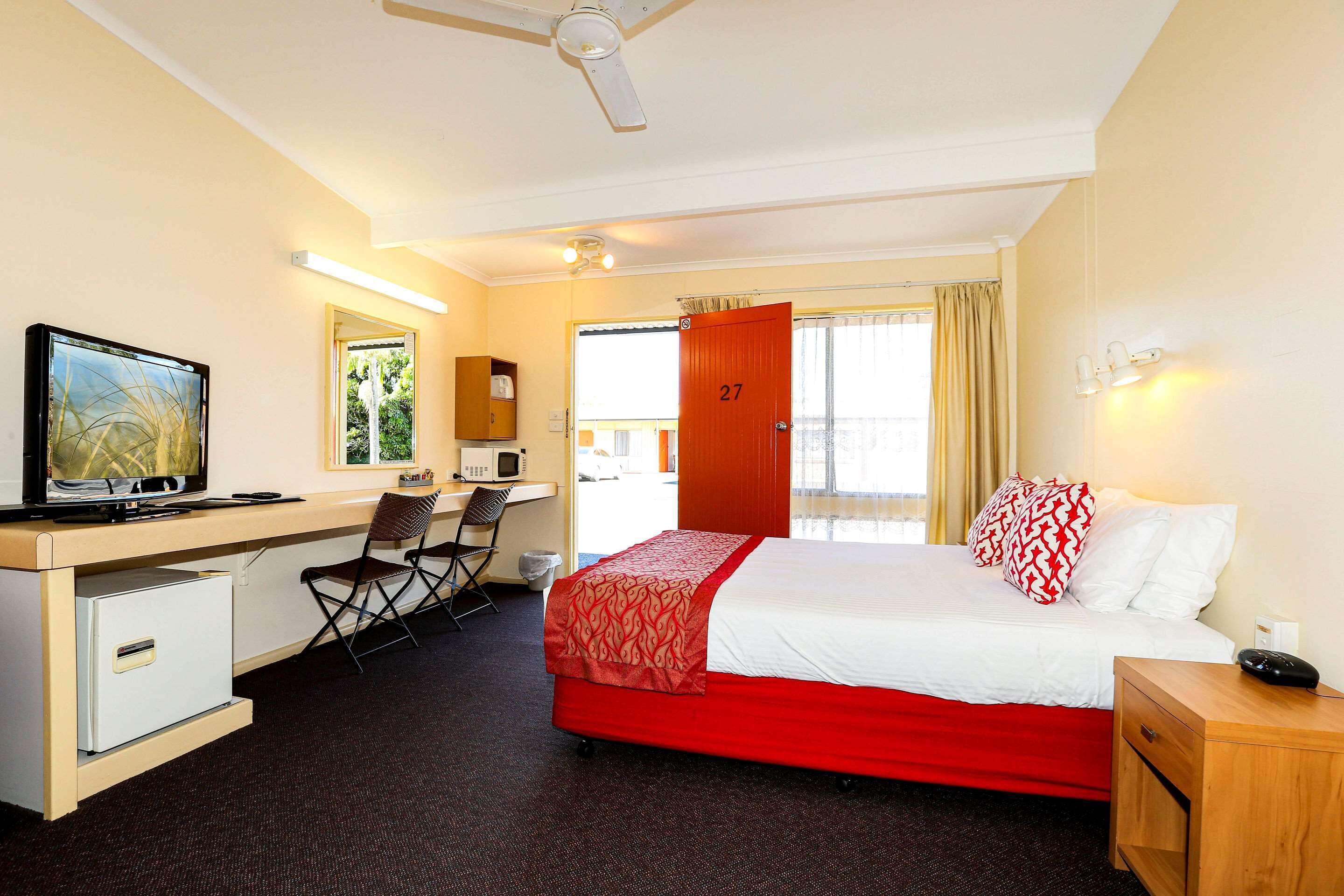 Quarto de hotel com cama, escrivaninha, cadeira, televisão e porta com o número 27.