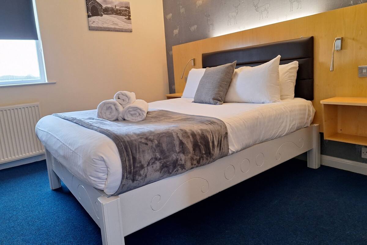 Quarto de hotel com uma cama, um quadro na parede, uma mesa de cabeceira e uma janela.