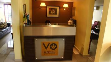 Bancada de recepção de hotel com tampo de vidro, uma moldura com imagem acima e duas luminárias fixadas na parede.