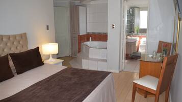 Quarto de hotel com cama, escrivaninha, cadeira, banheiro com banheira e espelho.