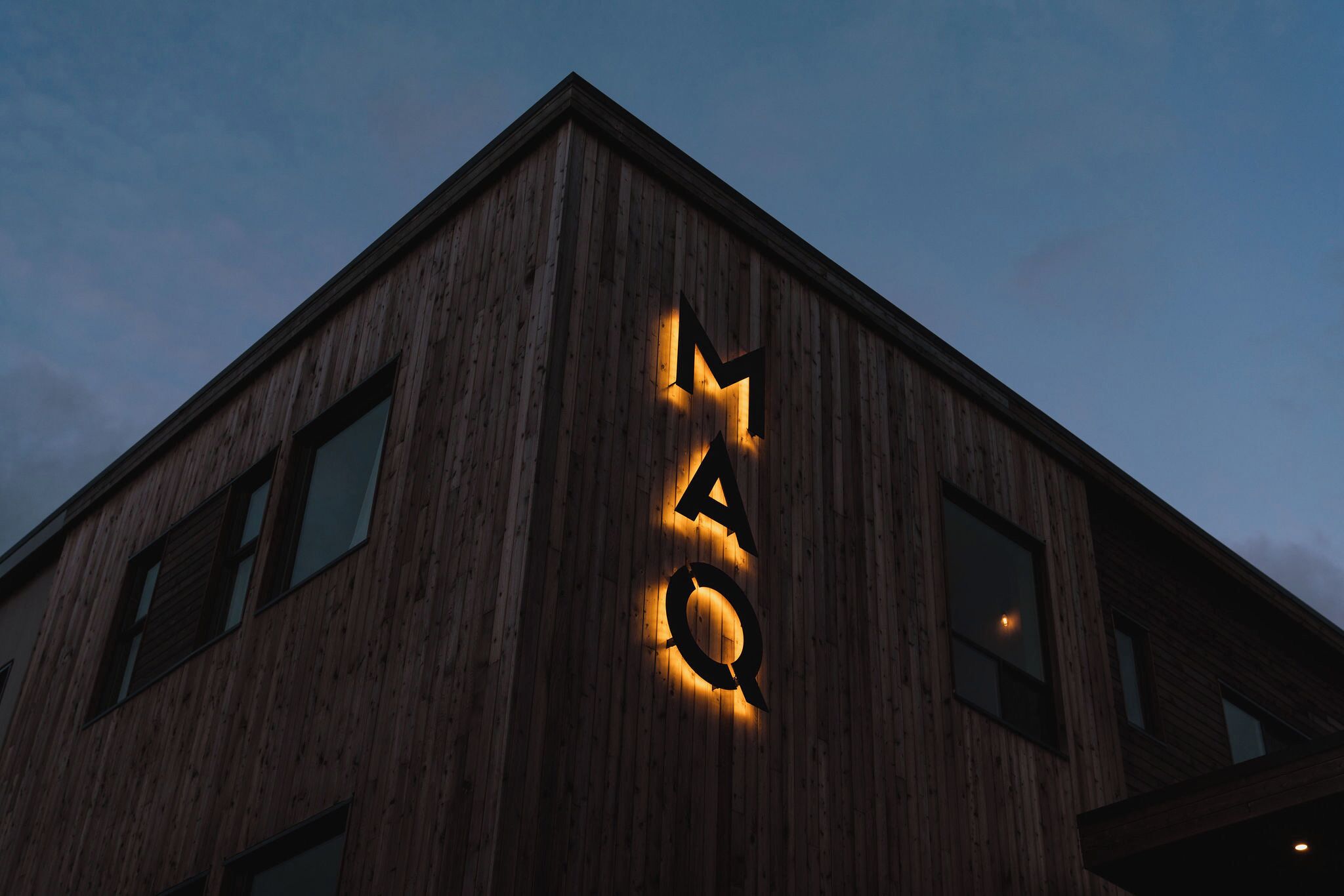 Um edifício com fachada de madeira e letras iluminadas que formam a palavra 'MACQ'.