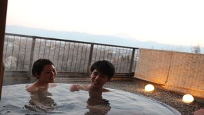 Duas pessoas em uma banheira de hidromassagem com vista para montanhas ao fundo.