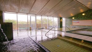 Piscina interna com paredes de vidro transparente, piso revestido e teto de madeira.