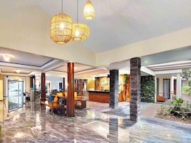 Um hall amplo com piso de mármore, pilares de madeira imponentes e luminárias pendentes.