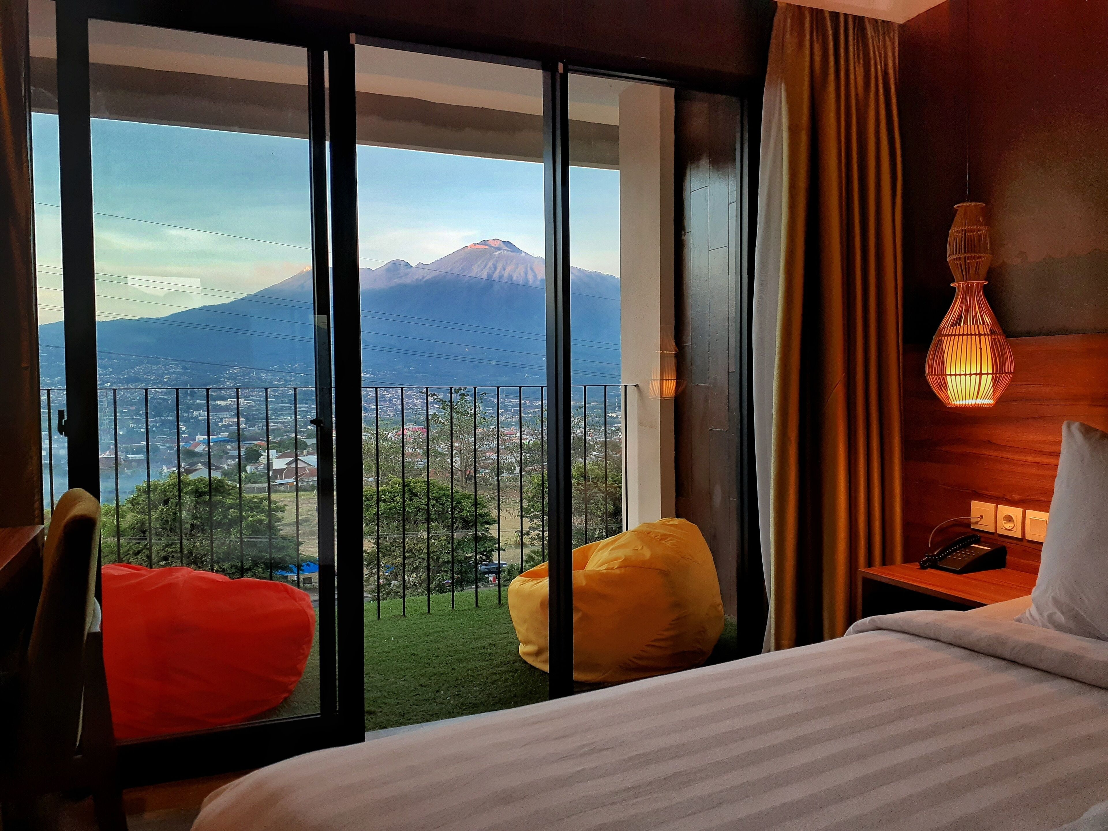 Quarto de hotel com uma cama, uma cadeira, uma mesa de cabeceira, um abajur e vista para uma montanha.