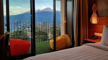 Quarto de hotel com uma cama, uma cadeira, uma mesa de cabeceira, um abajur e vista para uma montanha.