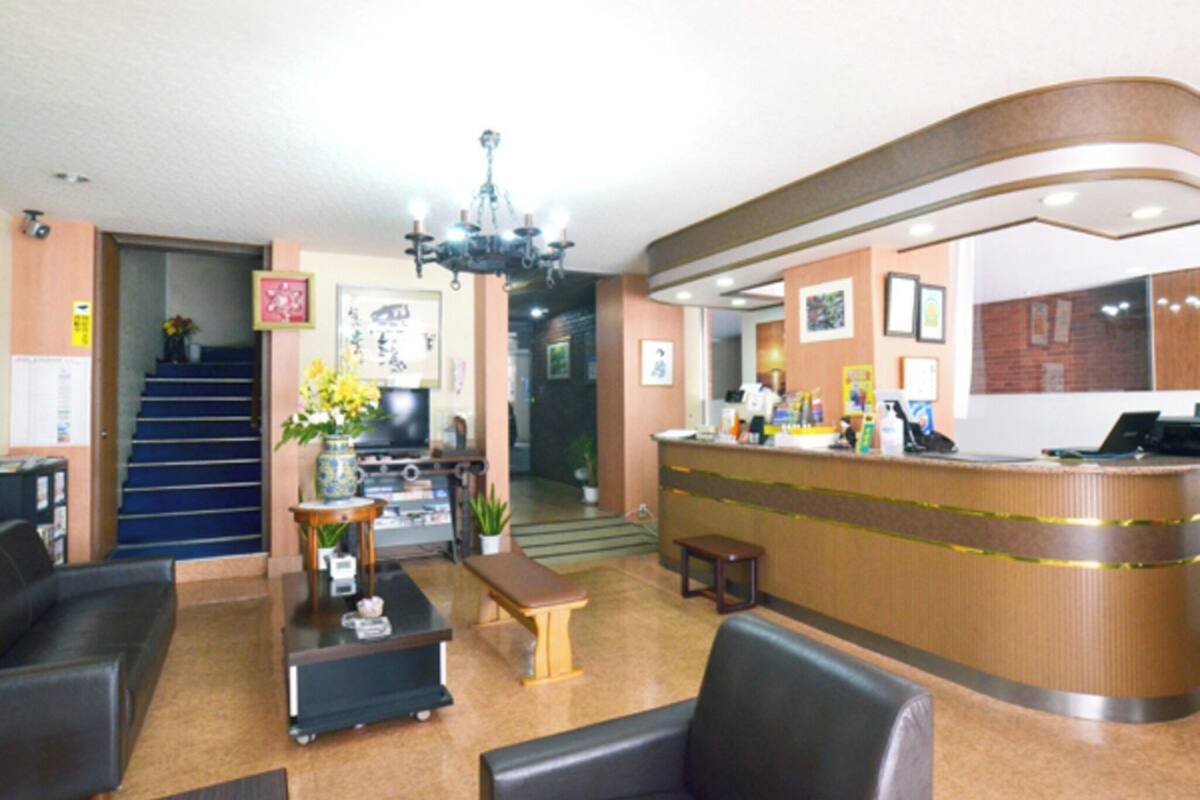 Um hall de hotel com balcão de recepção, área de estar, escadaria e um candelabro.