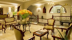 Um hall com balcão de recepção, escada e área de estar com cadeiras e uma mesa.