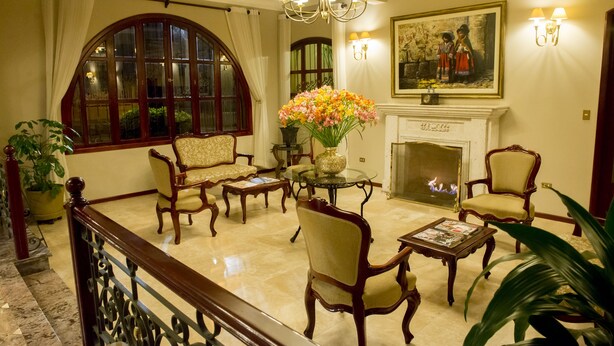 Uma sala de estar formal com lareira, um candelabro e móveis clássicos.
