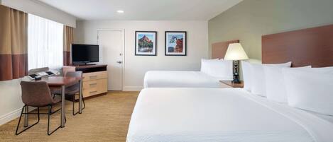 Quarto de hotel com duas camas, uma escrivaninha com cadeira, uma televisão e duas quadros na parede.