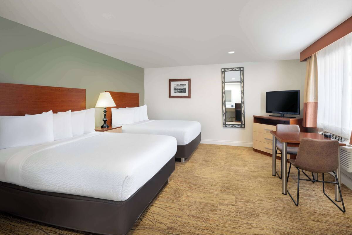Quarto de hotel com duas camas, uma escrivaninha com cadeira, televisão e espelho.