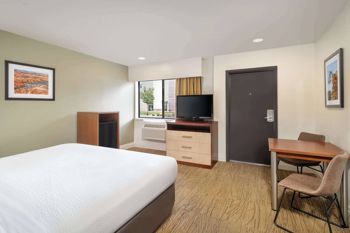 Quarto de hotel com uma cama, escrivaninha com cadeira, televisão e guarda-roupa.