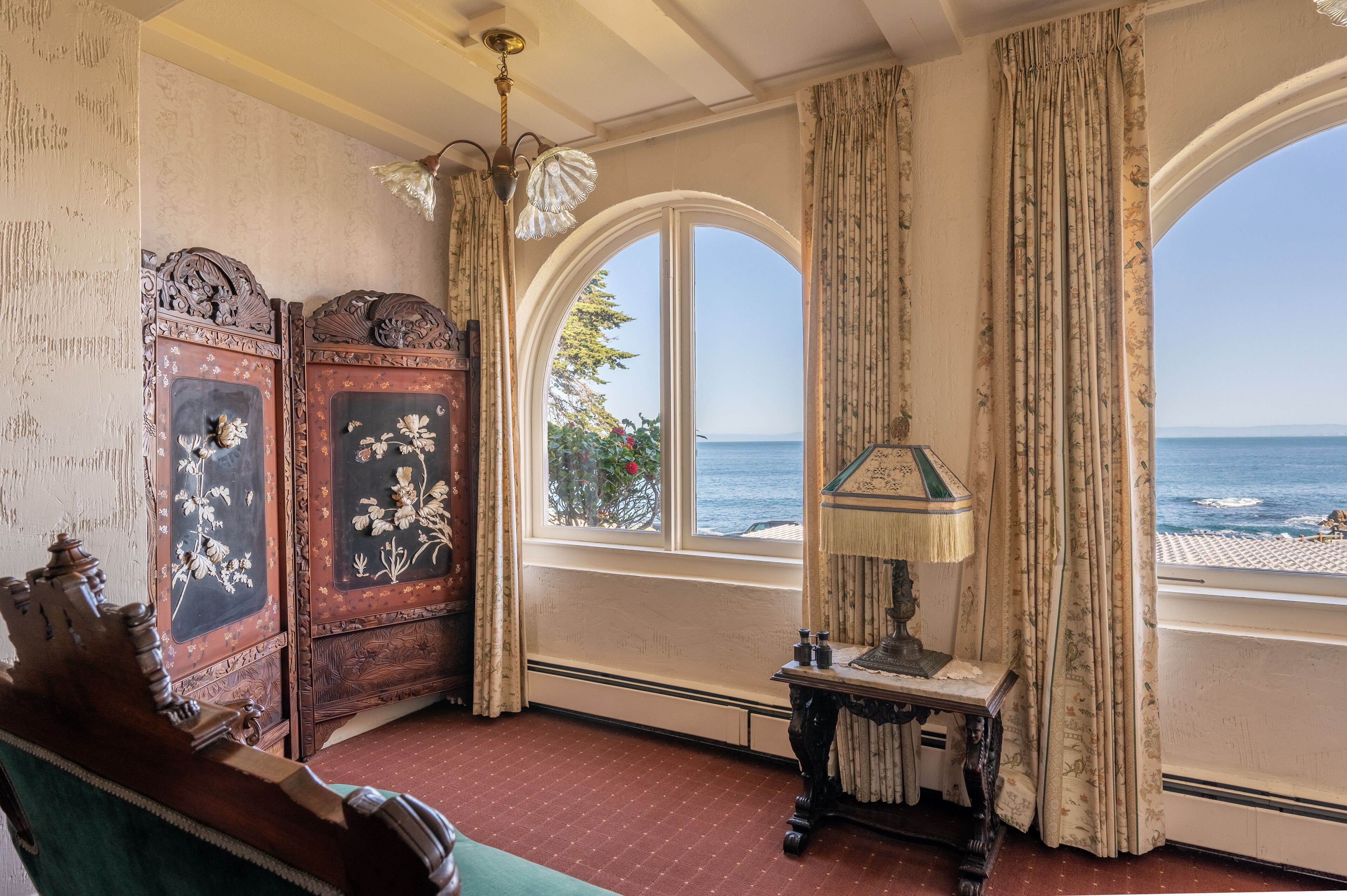 Quarto com uma grande janela arqueada, móveis de madeira ornamentados e vista para o mar.