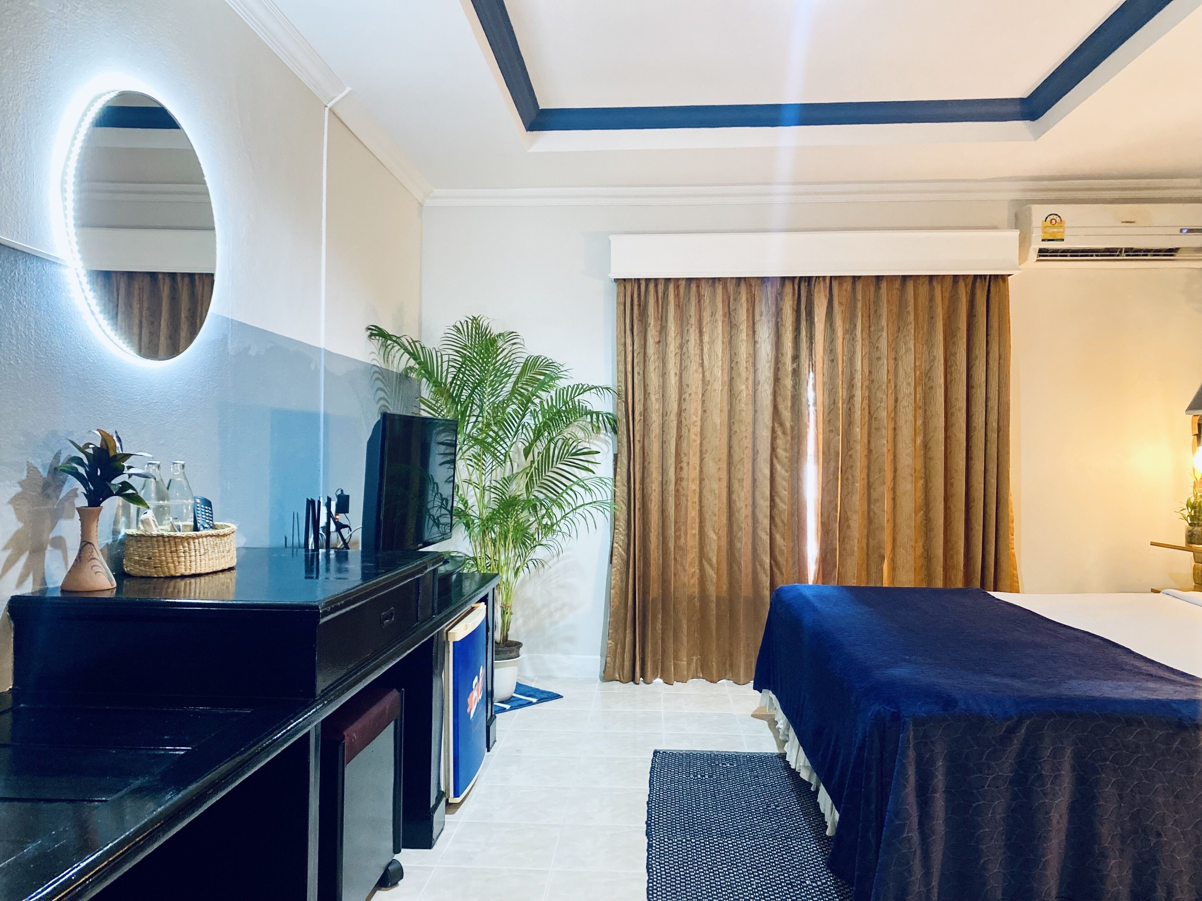 Quarto de hotel com cama, televisão em móvel, planta em vaso, espelho e janela com cortinas.