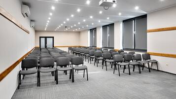 Uma sala de conferência com fileiras de cadeiras, um projetor e grandes janelas.