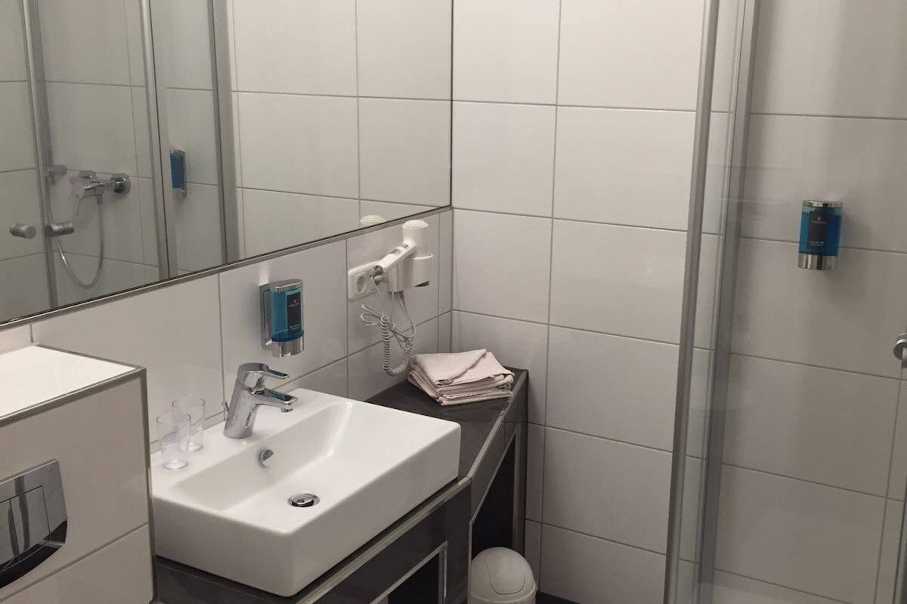 Casa de banho moderna com lavatório branco, espelho e cabine de duche em vidro.