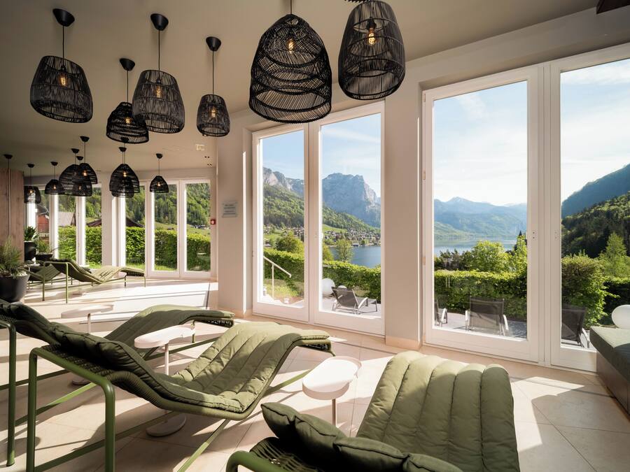 Quarto moderno com grandes janelas, poltronas de estar verdes e luminárias pendentes pretas.