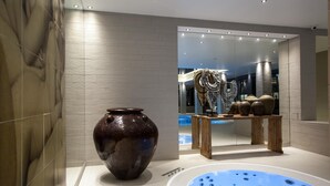 Uma casa de banho moderna com um grande vaso de cerâmica, uma mesa de madeira com objetos decorativos eum banheira de hidromassagem.