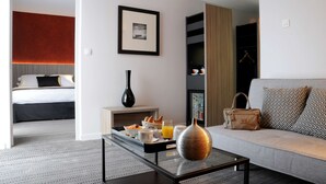 Quarto de hotel moderno com cama, sofá, mesa de centro com itens de café da manhã, quadro emoldurado e guarda-roupa.
