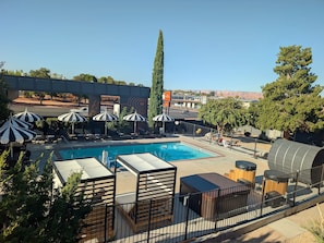 Área de piscina com espreguiçadeiras e guarda-sóis, uma árvore alta e vista da paisagem ao redor.