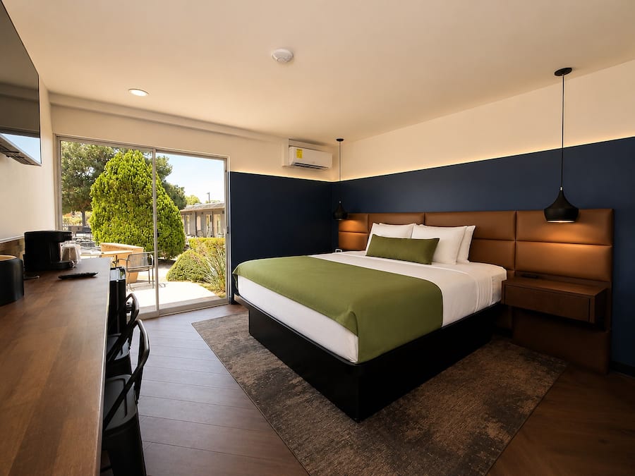 Quarto de hotel moderno com uma cama grande, uma escrivaninha e vista para o exterior.