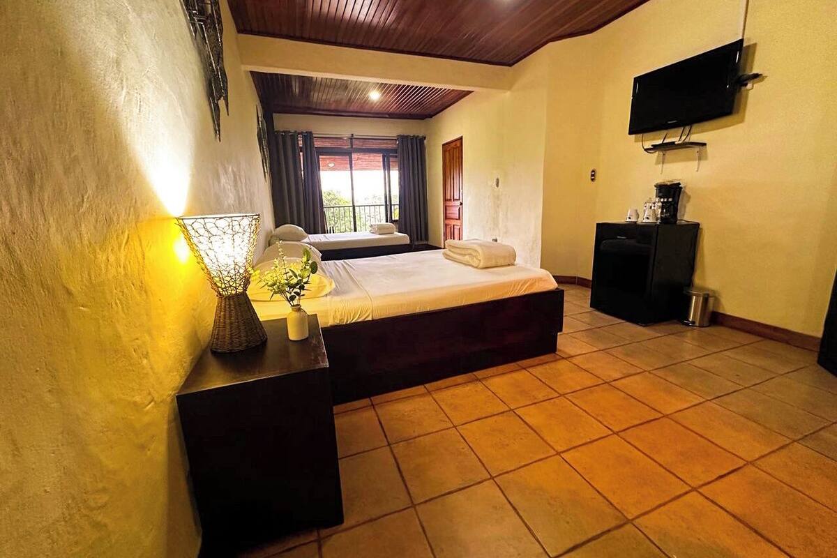 Um quarto com uma cama, uma escrivaninha, uma televisão e uma janela com cortinas.