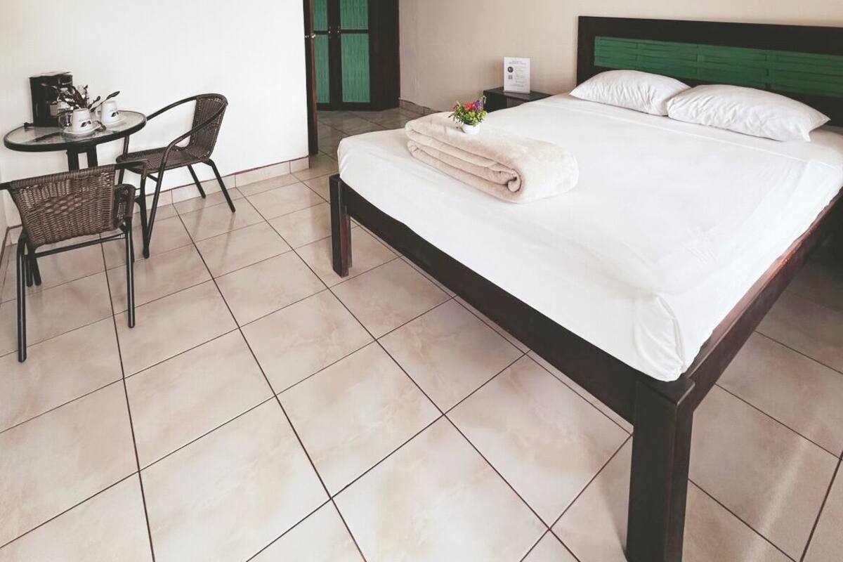 Quarto de hotel com cama, cadeira, mesa, ventilador de teto e um quadro na parede.