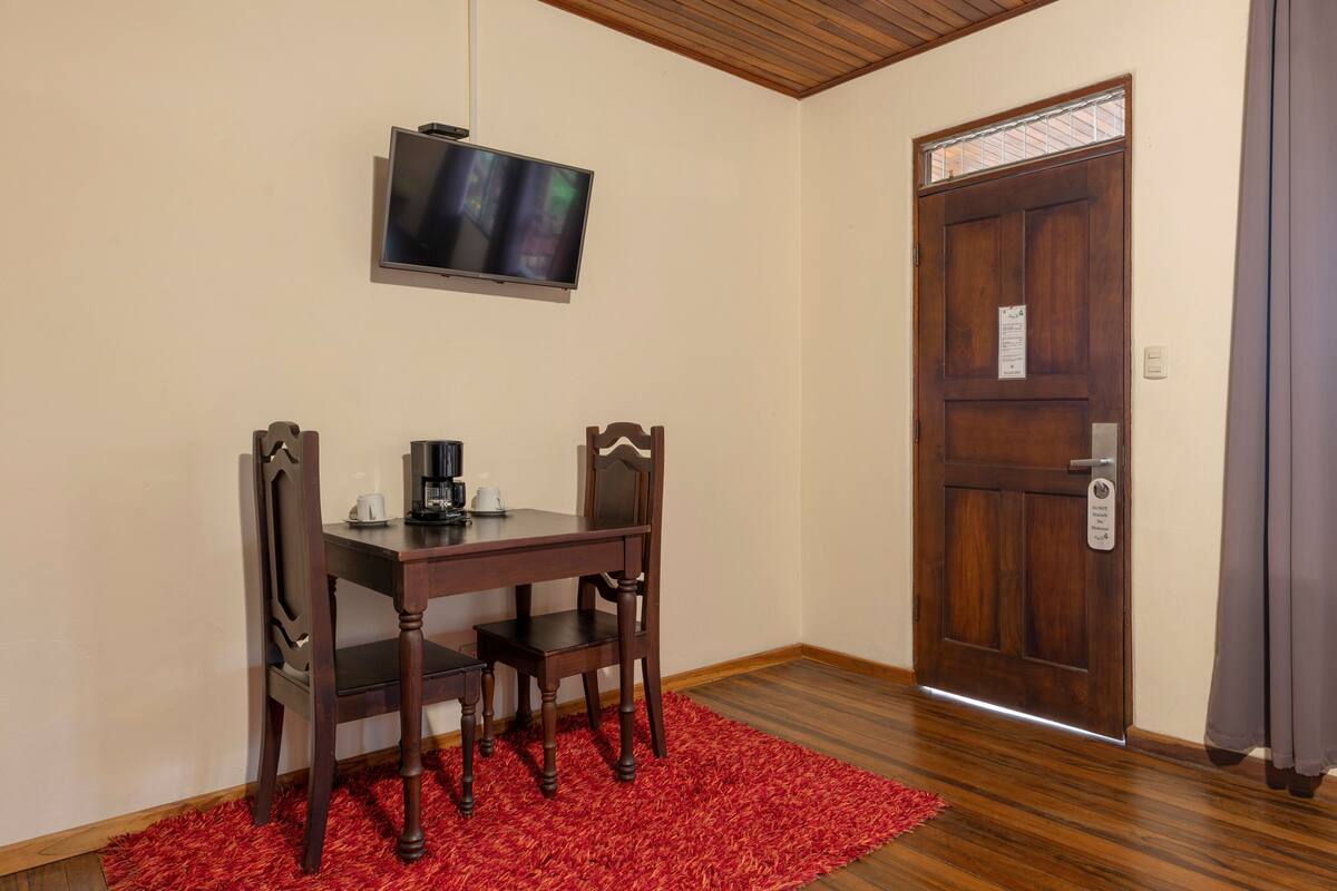Uma sala de jantar com mesa de madeira, cadeiras, uma televisão fixada na parede e uma porta de madeira com janela.