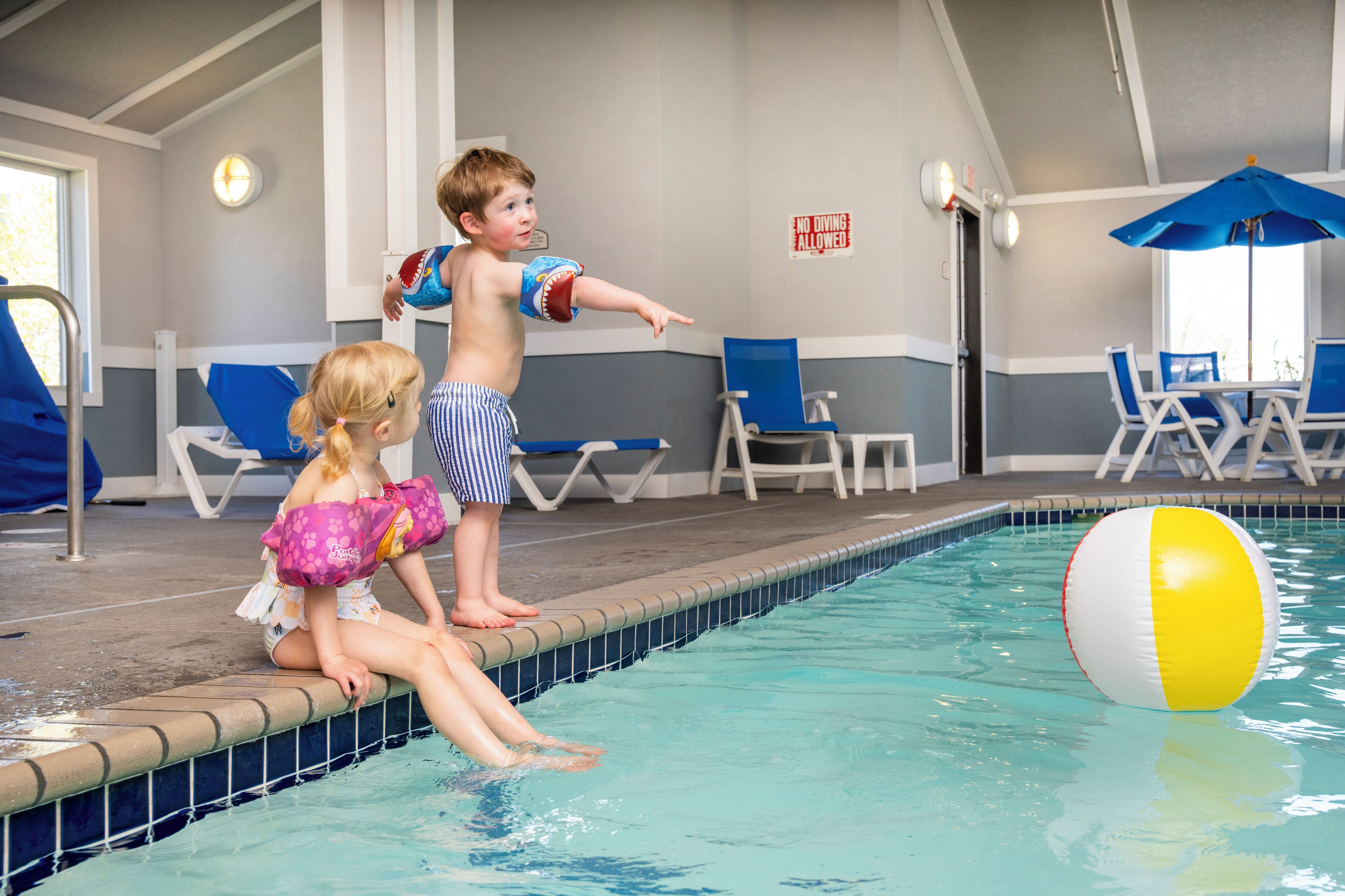 Uma área de piscina com trampolim, espreguiçadeiras e uma boia.