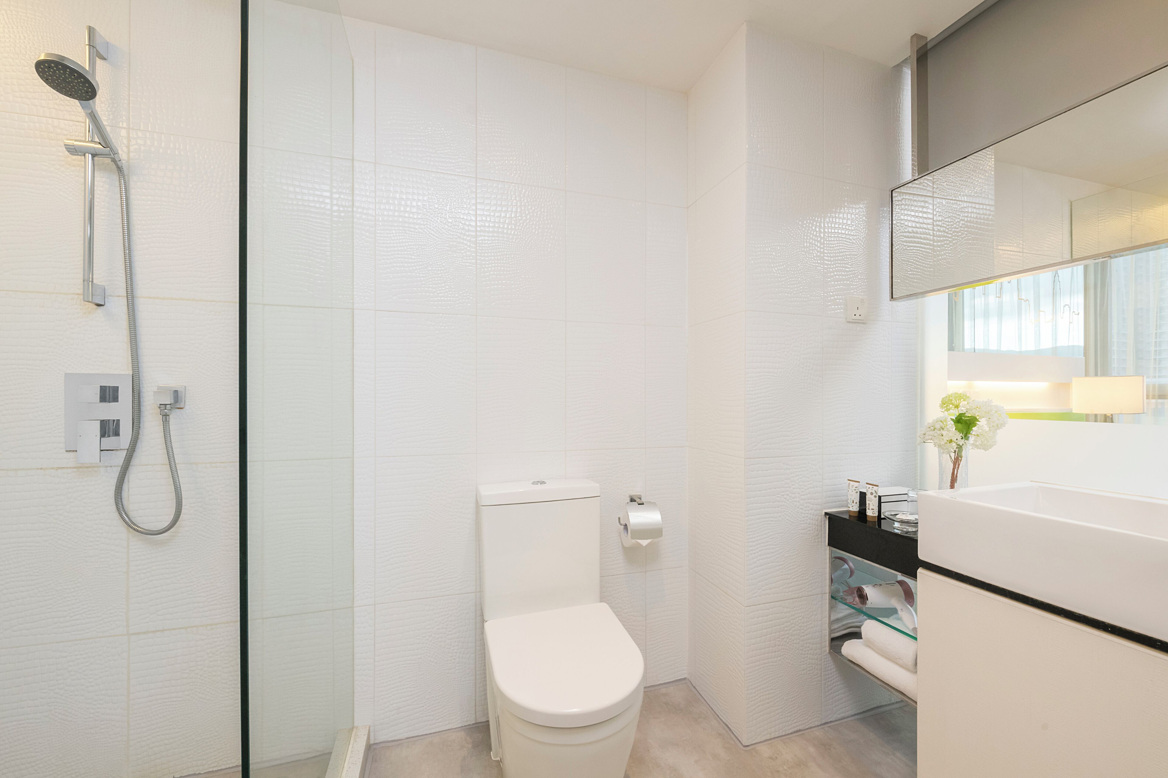 Um banheiro moderno com box de vidro, vaso sanitário branco e toucador com espelho.