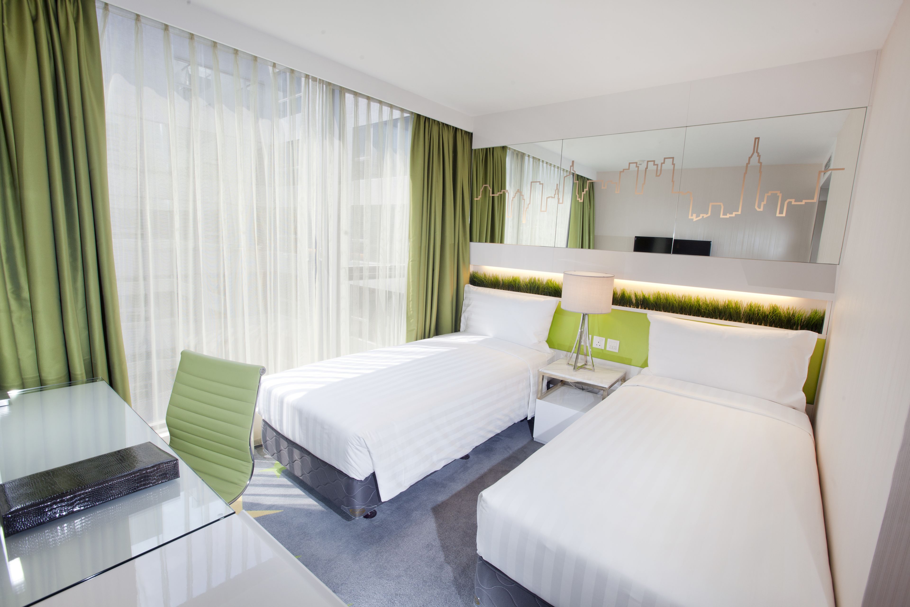 Quarto de hotel com duas camas, uma escrivaninha de vidro, uma cadeira, uma mesa de cabeceira com abajur e um espelho grande com design de paisagem urbana.