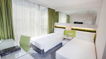 Quarto de hotel com duas camas, uma escrivaninha de vidro, uma cadeira, uma mesa de cabeceira com abajur e um espelho grande com design de paisagem urbana.