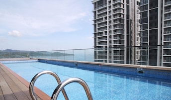 Piscina no terraço com água azul cristalina, rodeada por um deck de madeira e corrimãos de metal. Ao fundo, visível um edifício moderno com varandas.