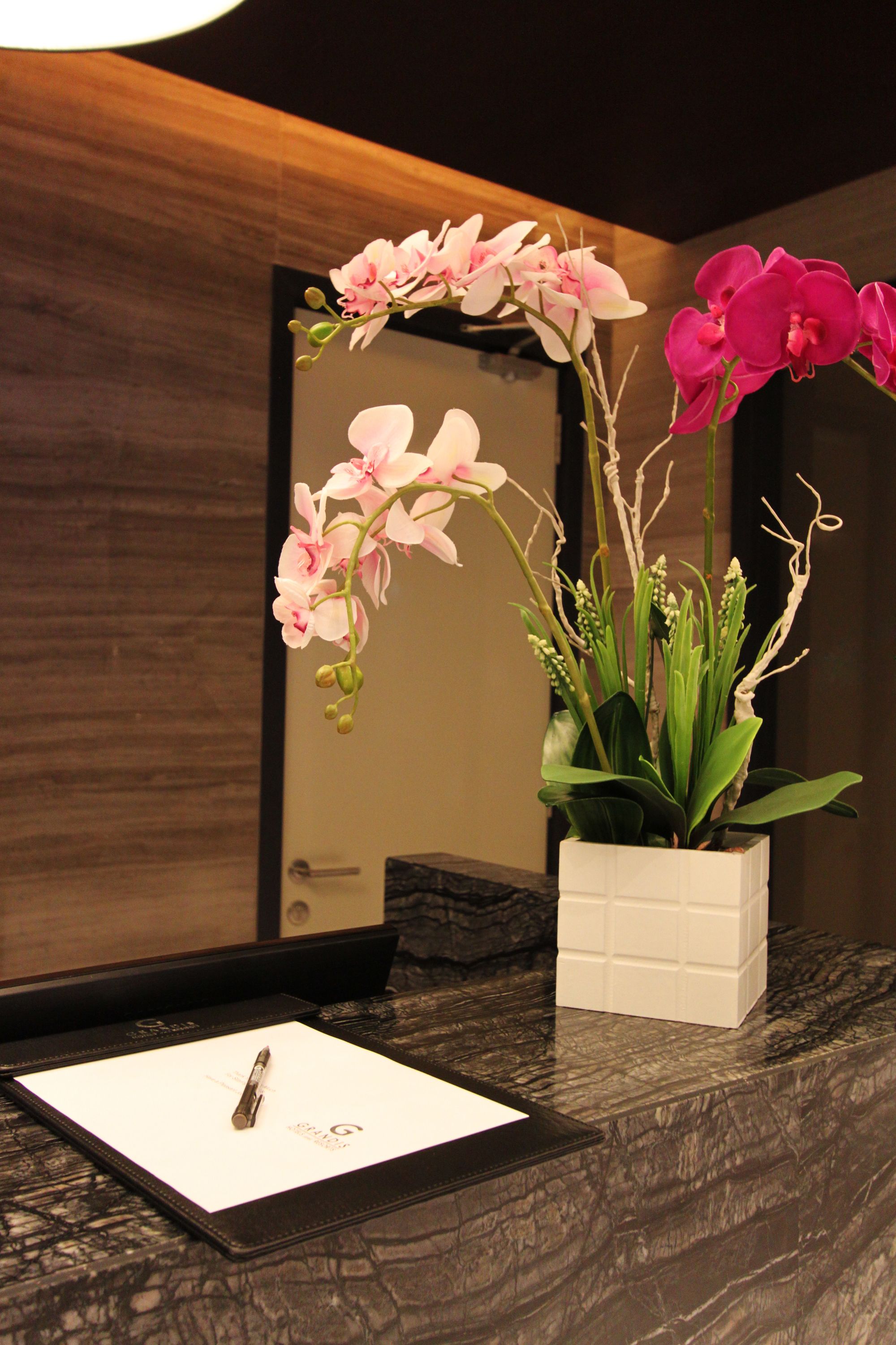 Uma bancada de mármore com um vaso branco contendo orquídeas rosa e roxas.