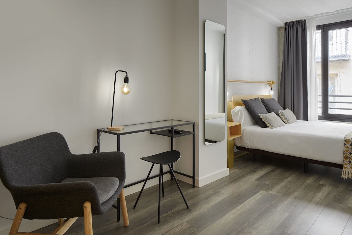 Quarto de hotel moderno com uma cama, uma mesa, uma cadeira e um abajur.