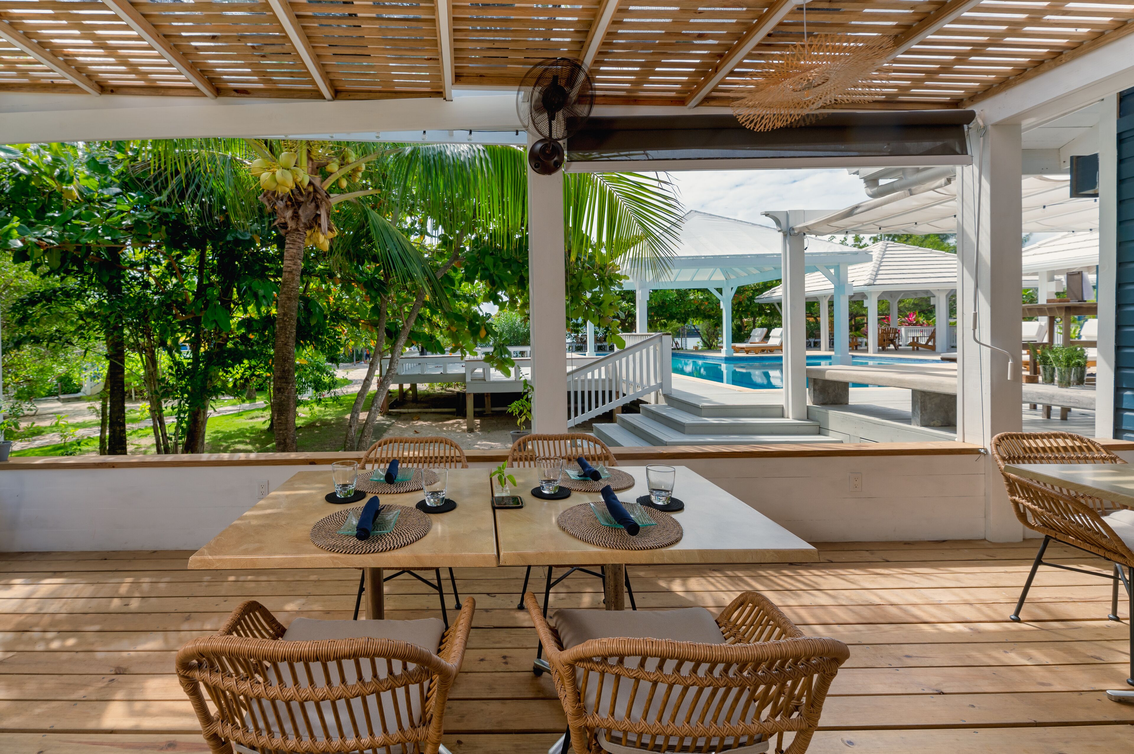 Um pátio externo com mesas e cadeiras de vime, com vista para uma piscina e vegetação exuberante.