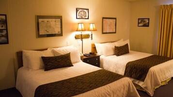 Quarto de hotel com duas camas, mesa de cabeceira com abajures e quadros decorativos nas paredes.