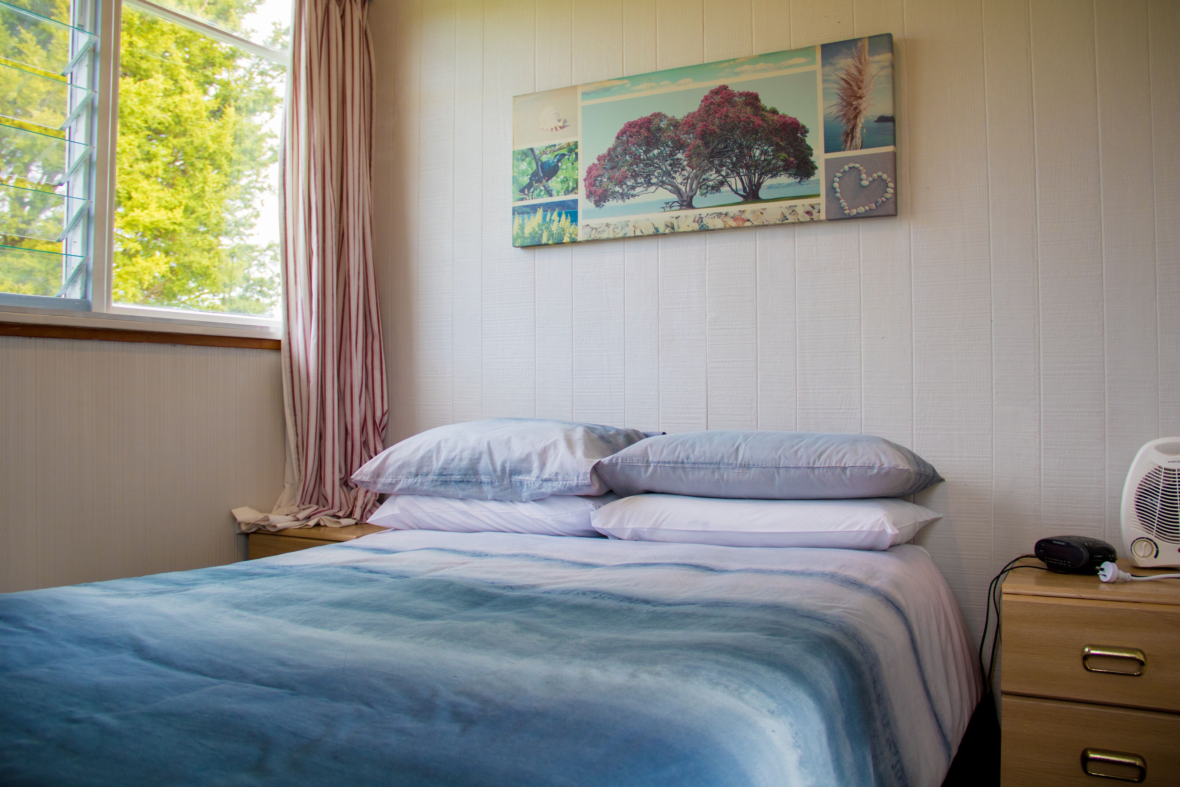 Quarto com cama, mesa de cabeceira, quadro na parede e janela com cortinas.