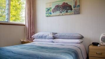 Quarto com cama, mesa de cabeceira, quadro na parede e janela com cortinas.