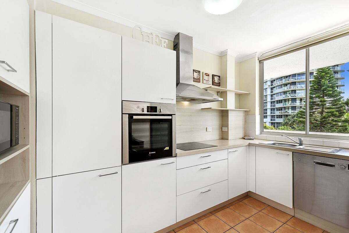 Uma cozinha moderna com armários brancos, forno embutido e janela com vista para um edifício alto.