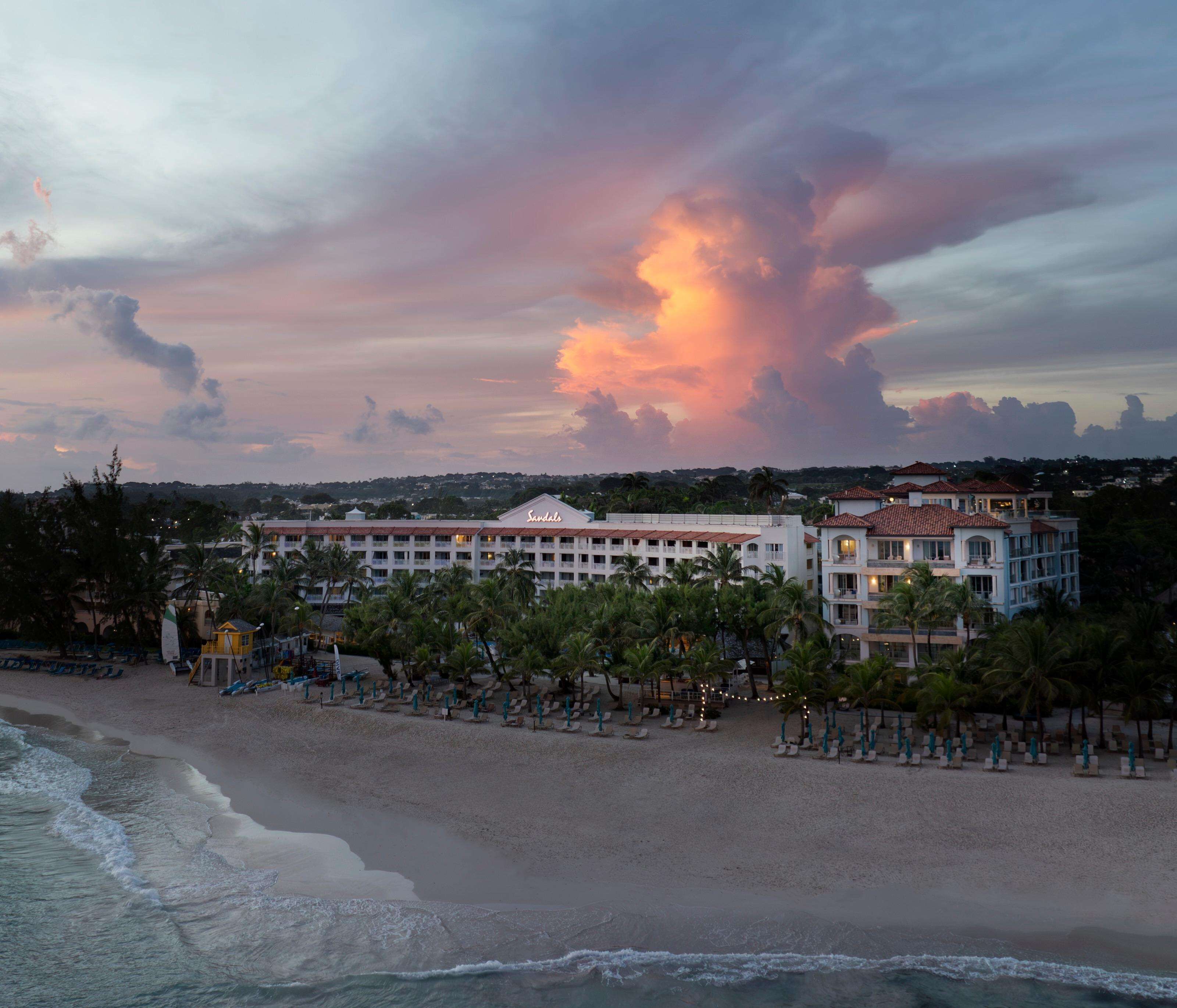 Hotel à beira-mar com vários edifícios, uma praia de areia e palmeiras.