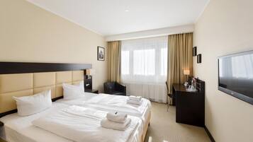 Quarto de hotel com duas camas, uma mesa, uma cadeira, televisão e janela com cortinas.