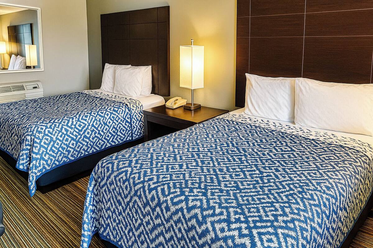 Quarto de hotel com duas camas, cada uma com colcha estampada, mesa de cabeceira com abajur e espelho na parede.