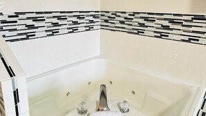 Casa de banho de canto com banheira branca, mosaicos preto e branco e um porta-toalhas com um frasco.